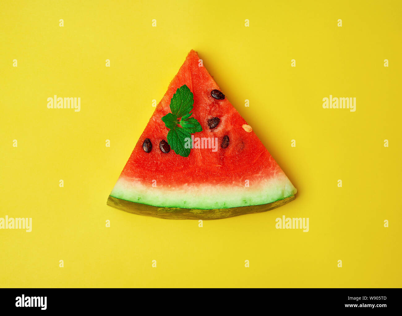 triangular slice of ripe red watermelon with seeds on a yellow ...