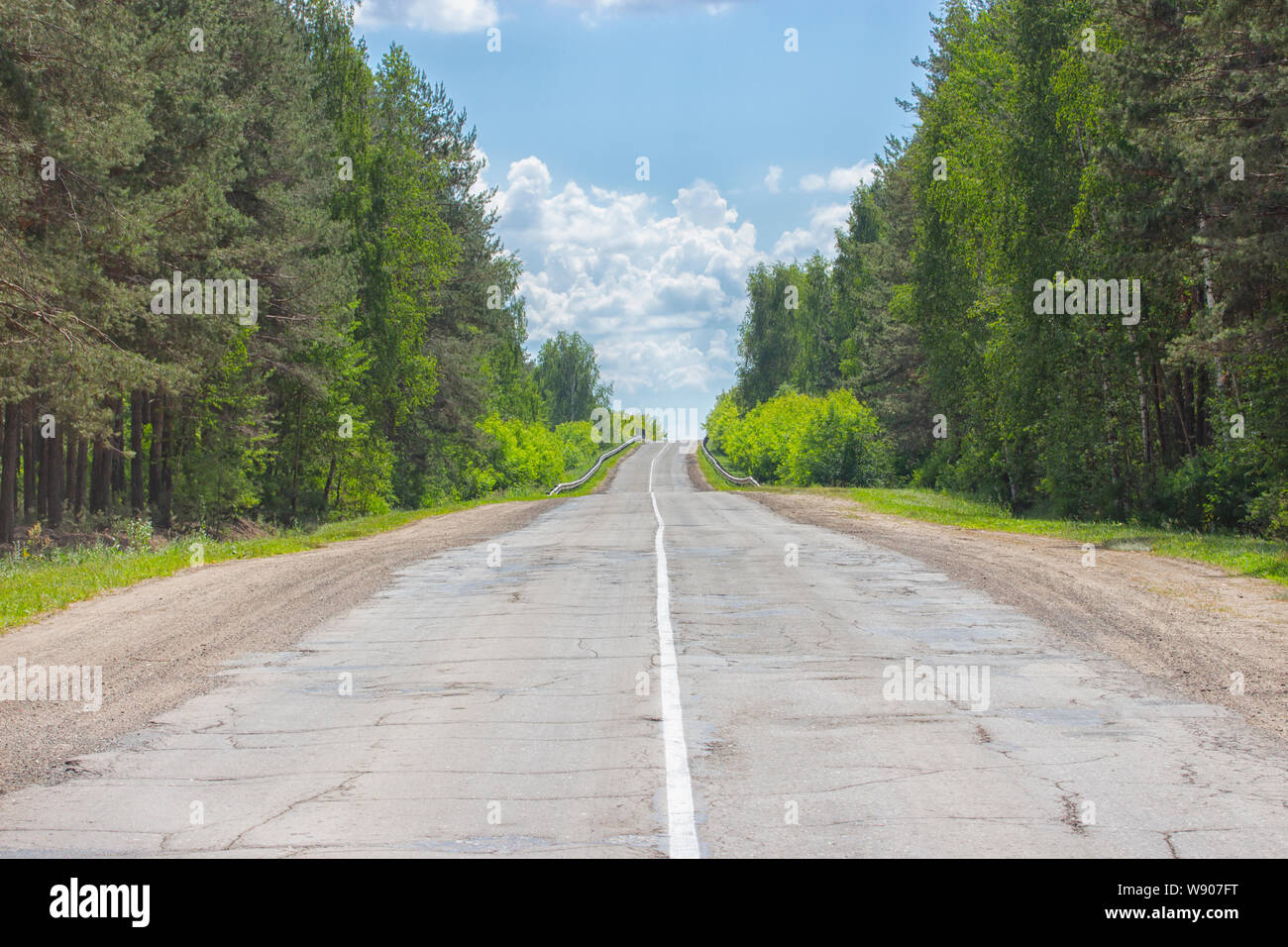 A poorly-paved rural two-lane road, deciduous forest, cloudy sky ...