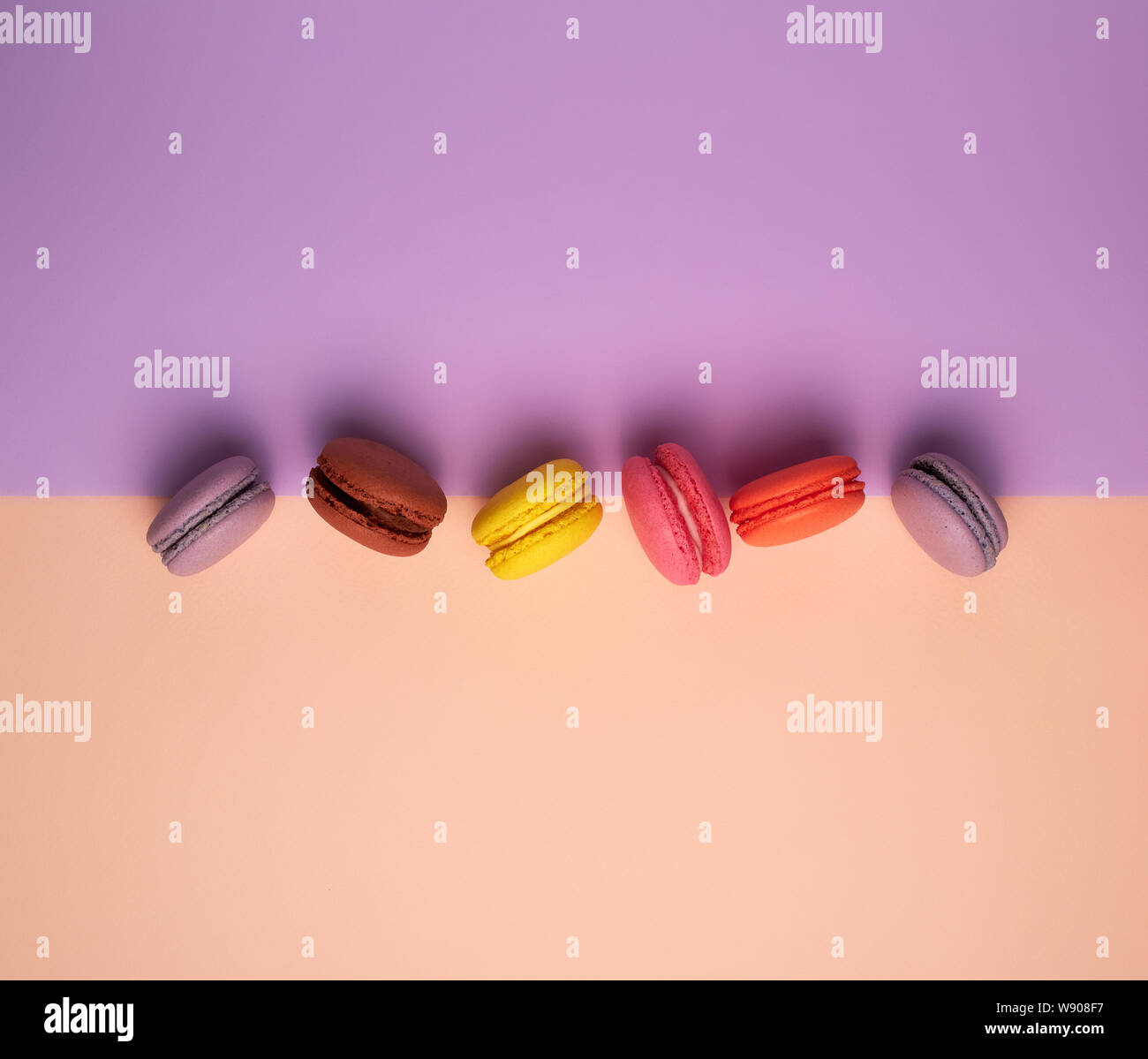 six multi-colored macarons with cream on a purple-beige background ...