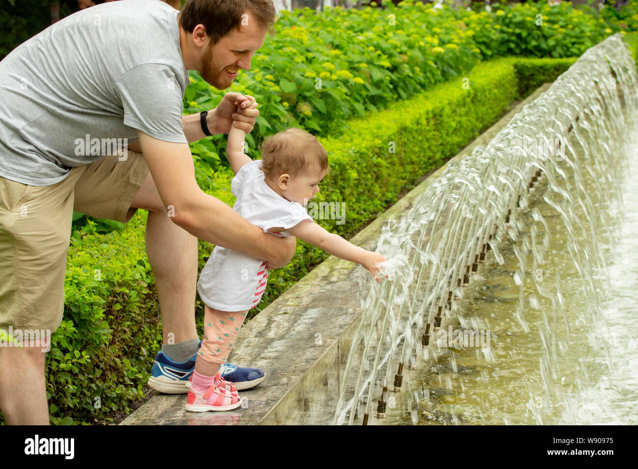 Dad walks with his little daughter in the park with fountains. Baby ...