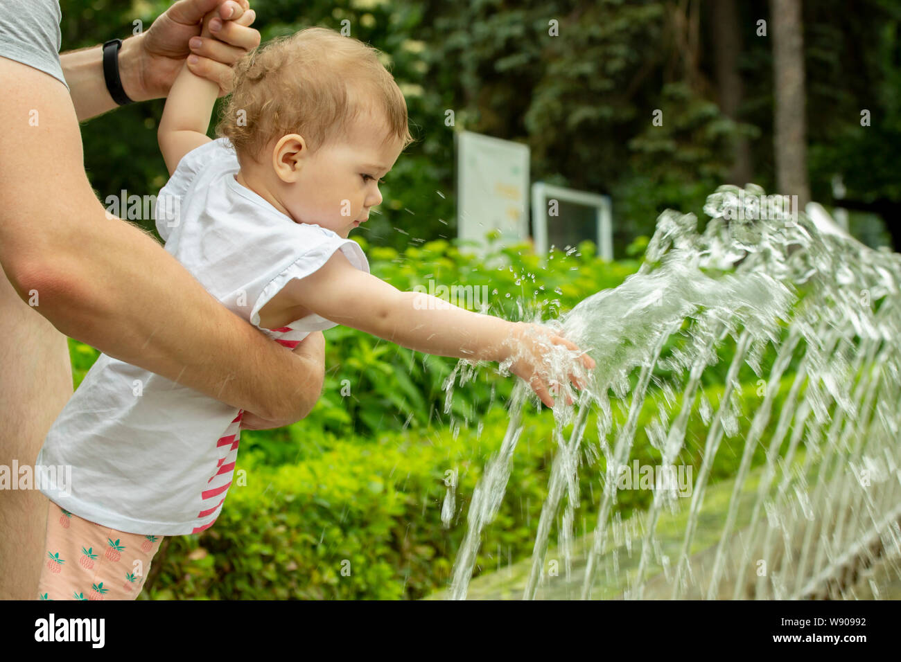 Baby girl playing with water in a fountain in the park. Little baby ...