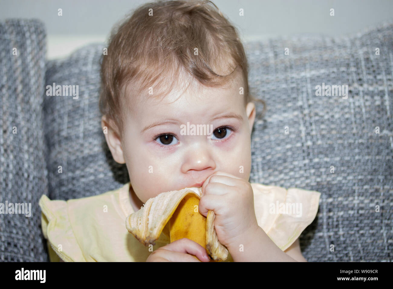 Baby girl eats banana, peels banana from skin. Portrait of a little ...