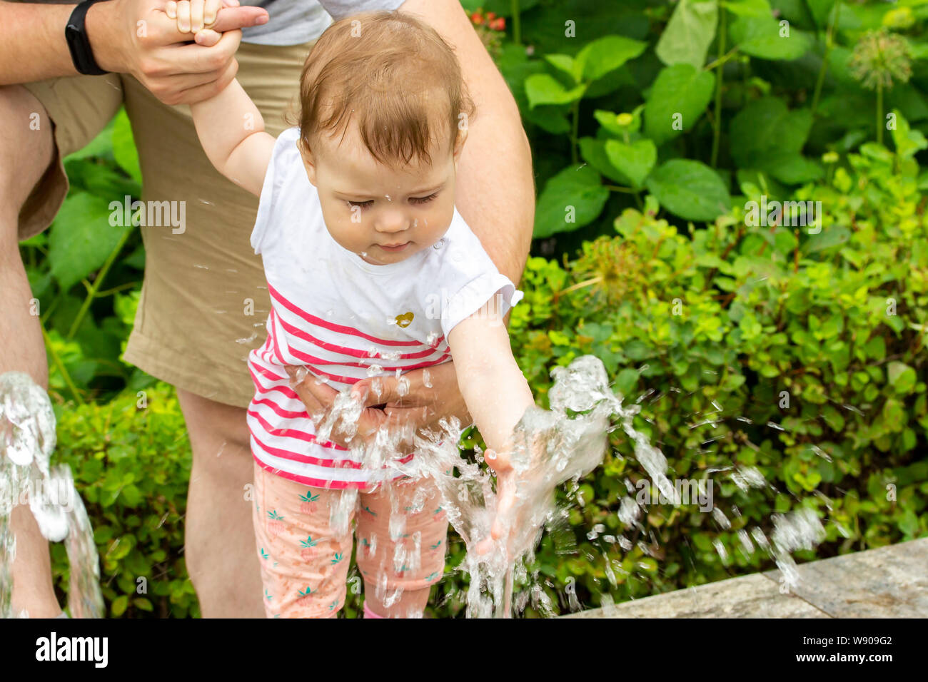 European baby girl playing with jets of water in a fountain. Baby wets ...