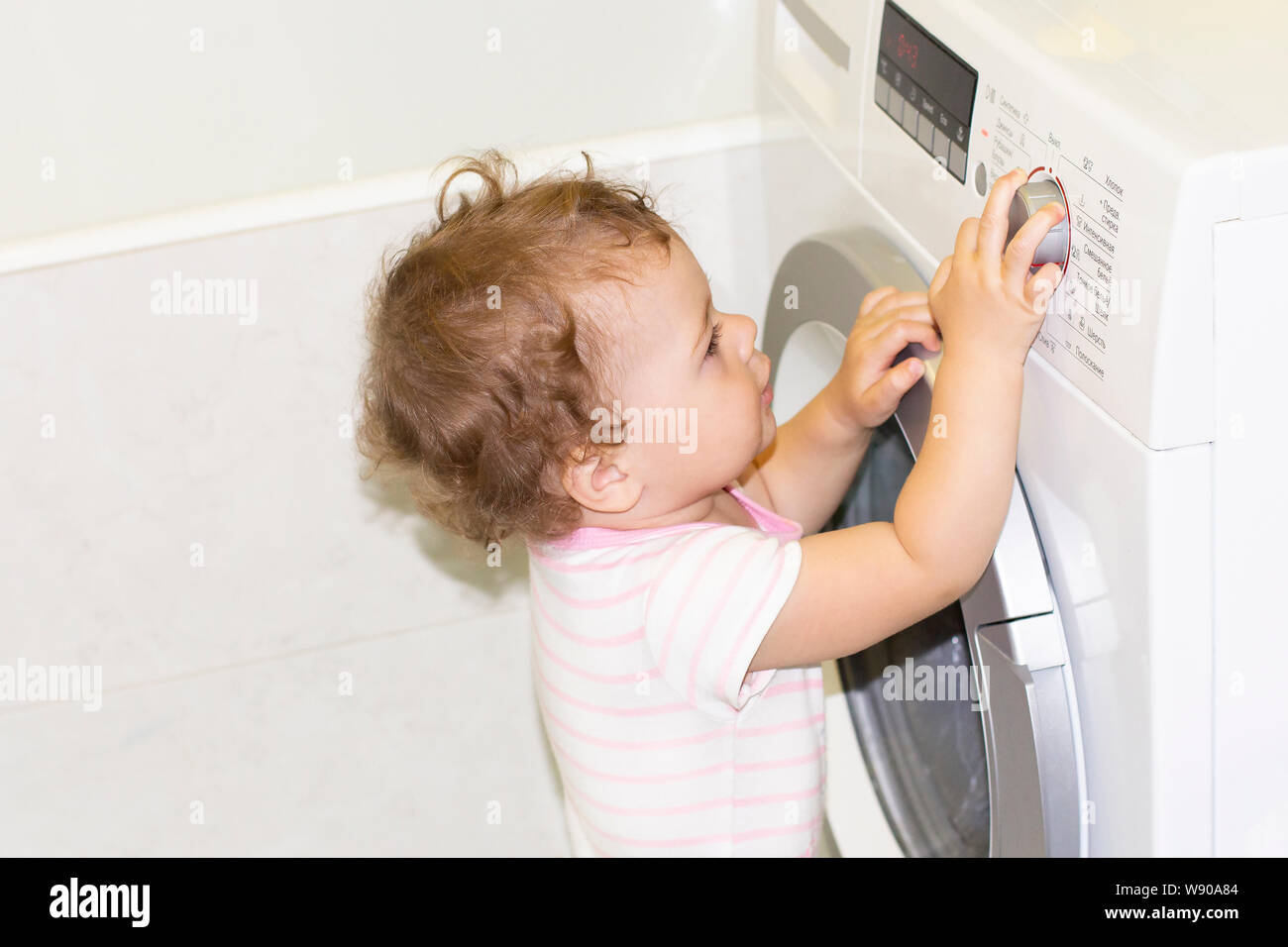 Little girl chooses a washing mode on a washing machine. Caucasian ...