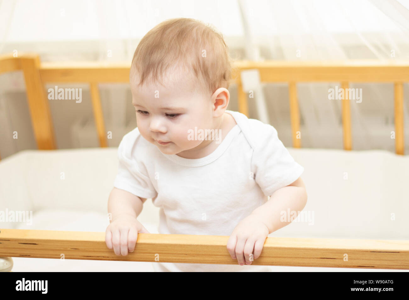 Baby 8 months in white looks out of the cradle. Cute baby knows the ...