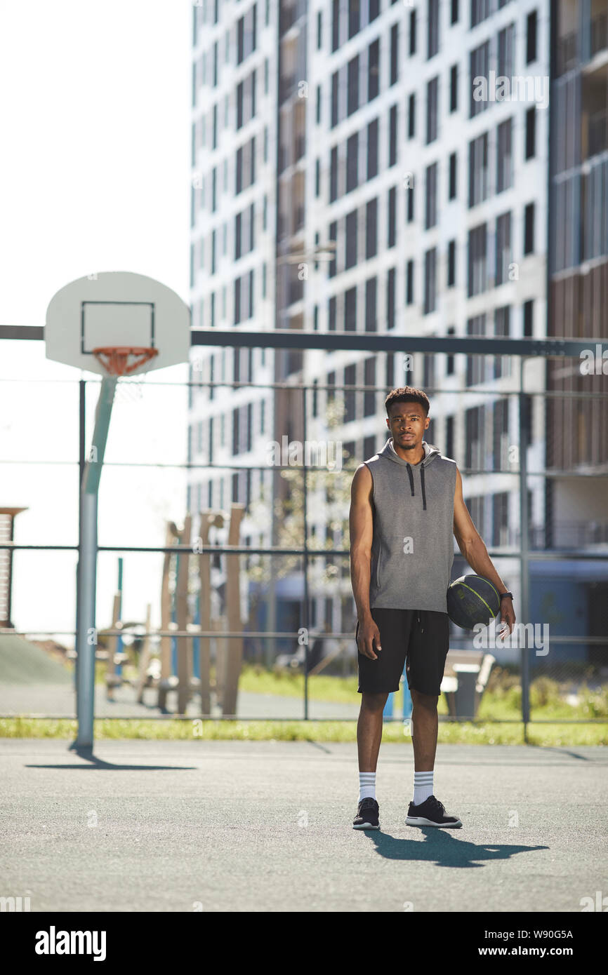 Full length portrait of African basketball player standing by hoop in ...