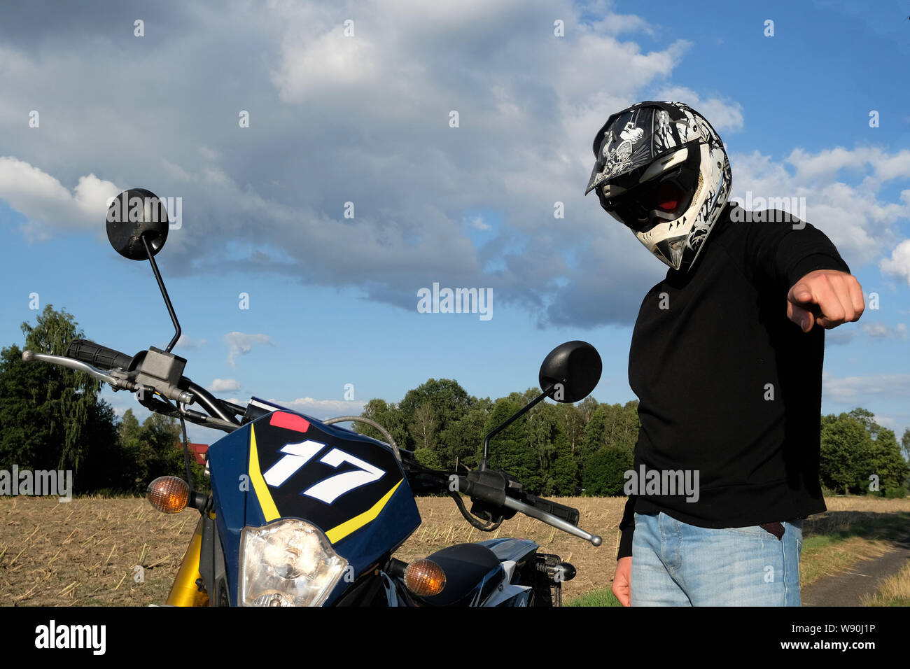 man with a motocycle in a helmet pointing finger on a country road ...