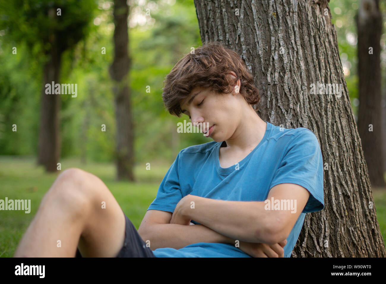 young male sleeping in the public park on the grass under the tree ...
