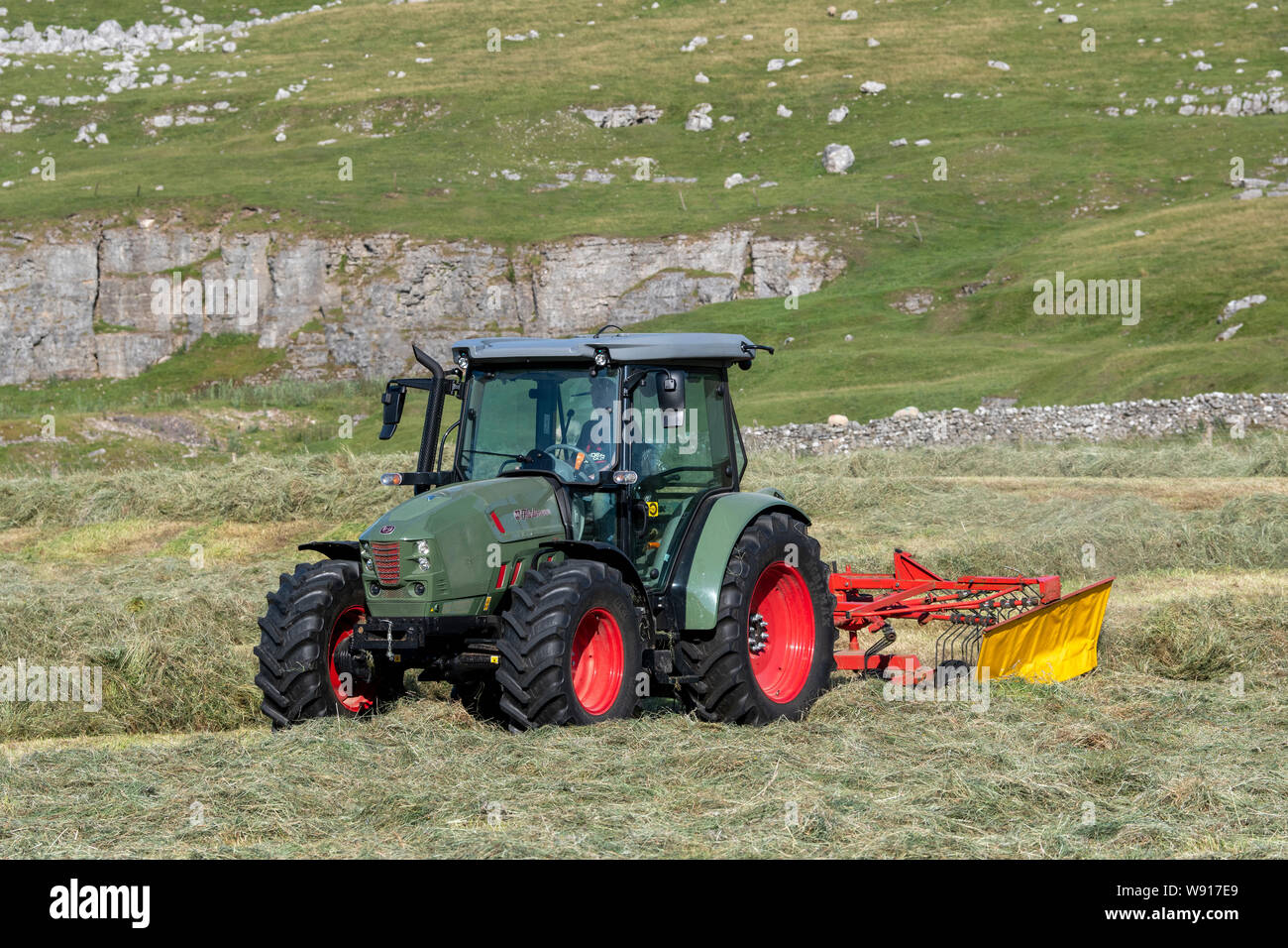 Farmer rowing up hay with a Hurlimann tractor and a two pass rake on a ...