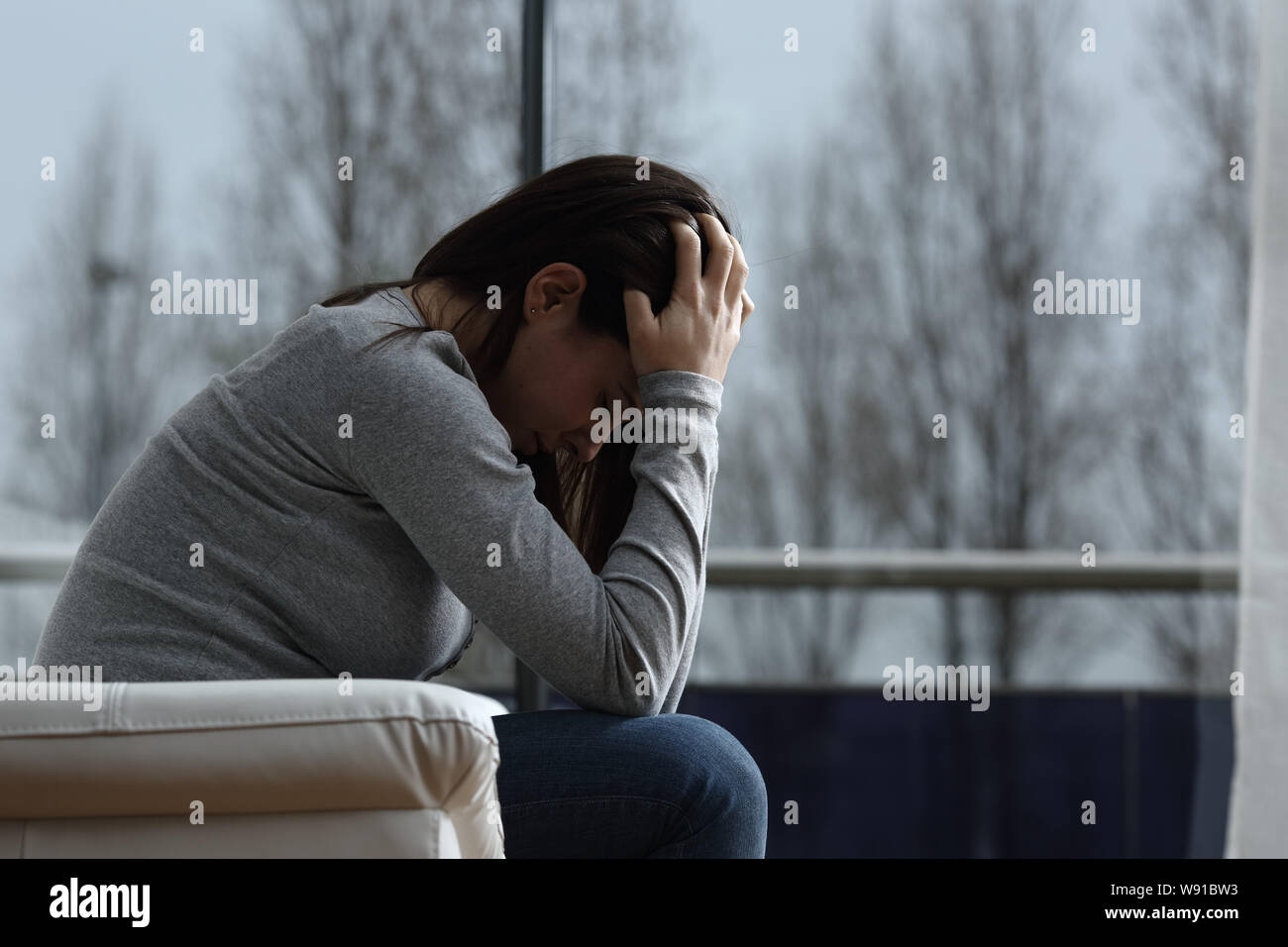 Side view portrait of a sad woman complaining alone sitting on a couch ...