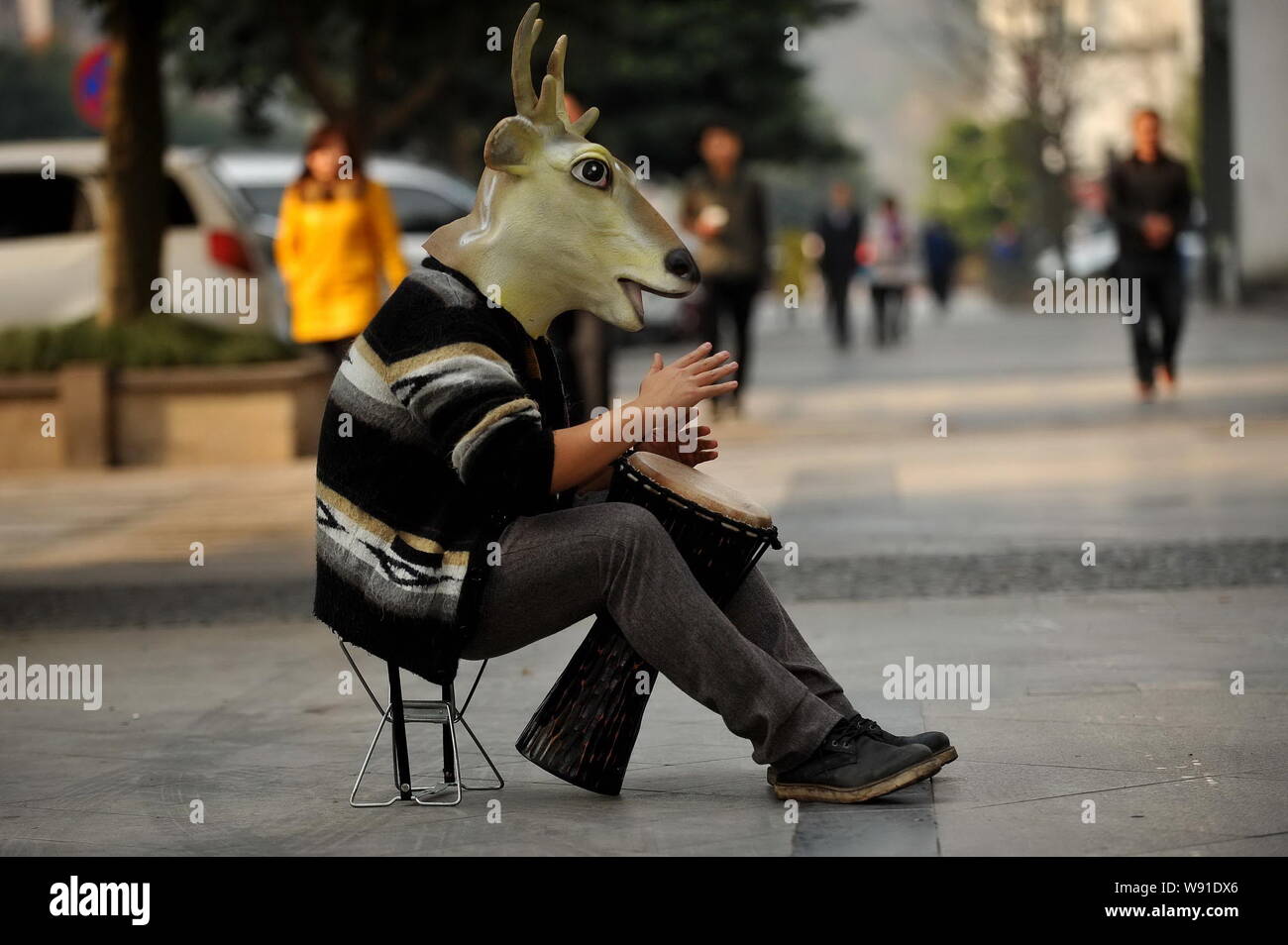 Luo Dan, wearing a big deer mask over his head, beats a drum on a ...