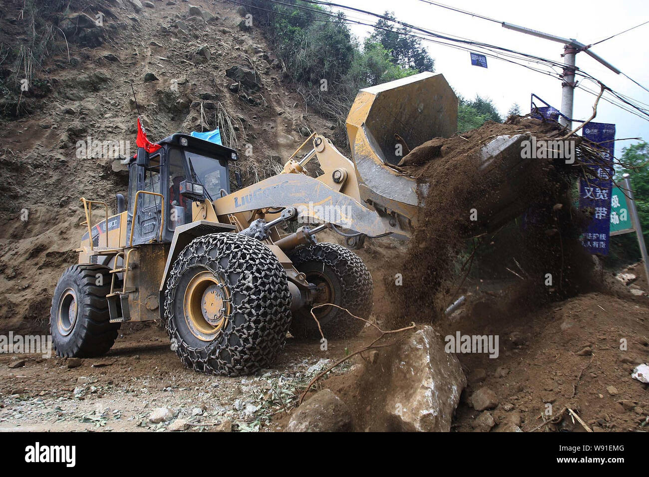 A worker drives a wheel loader to clear mud and rocks to make way on ...