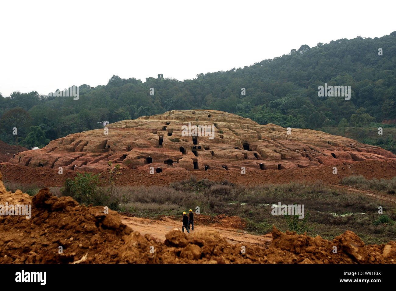 Workers walk past robbed ancient tombs on the slope of a hill in ...