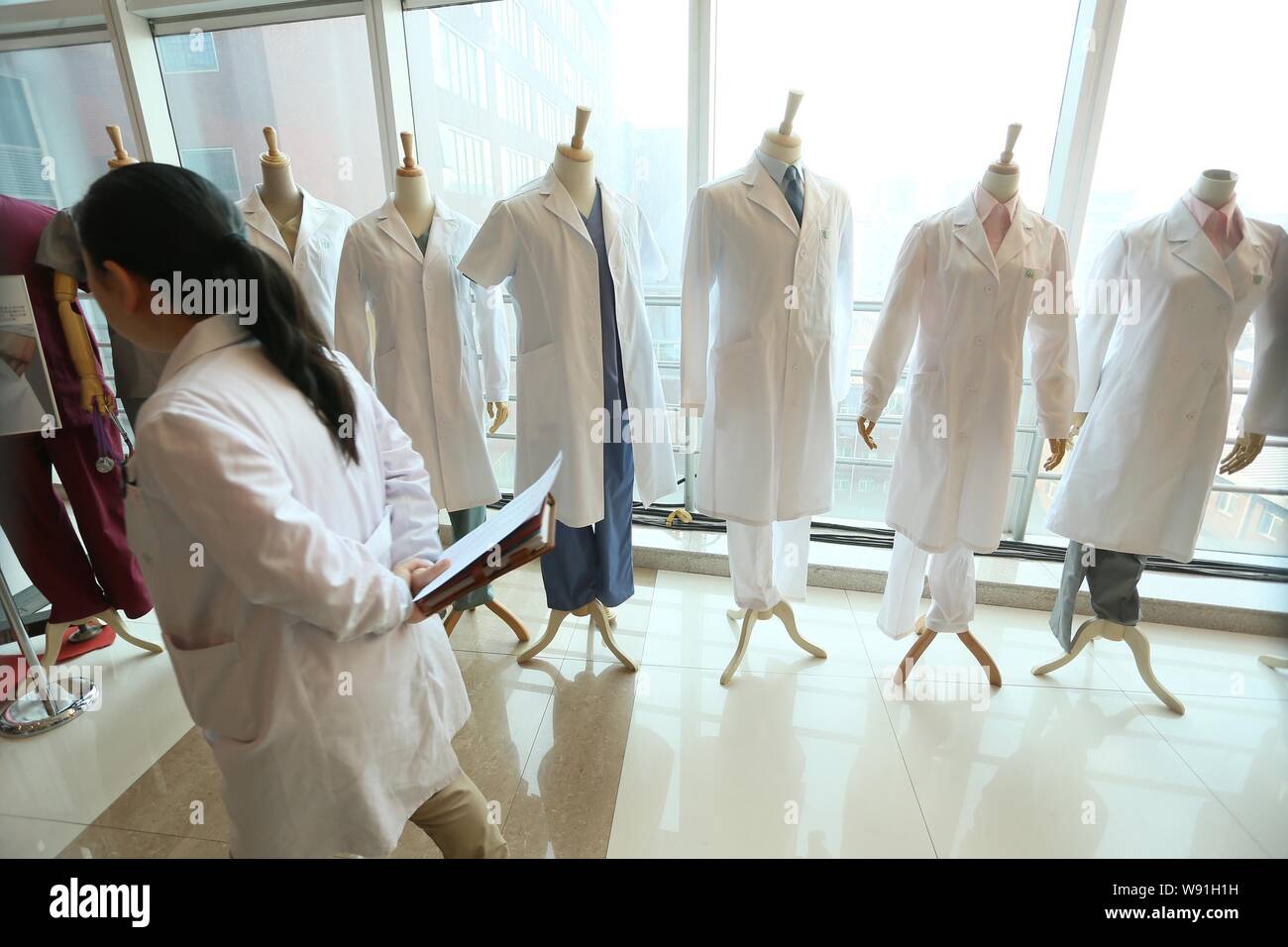 A Chinese doctor walks past new hospital uniforms on display during a ...