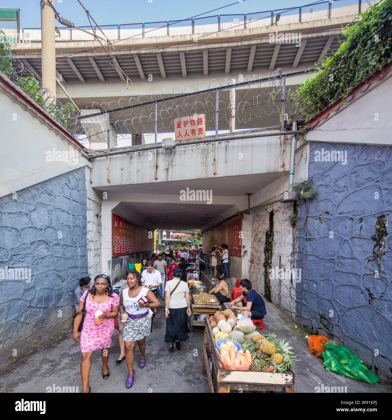 African people and local Chinese residents walk past stalls of fruit ...