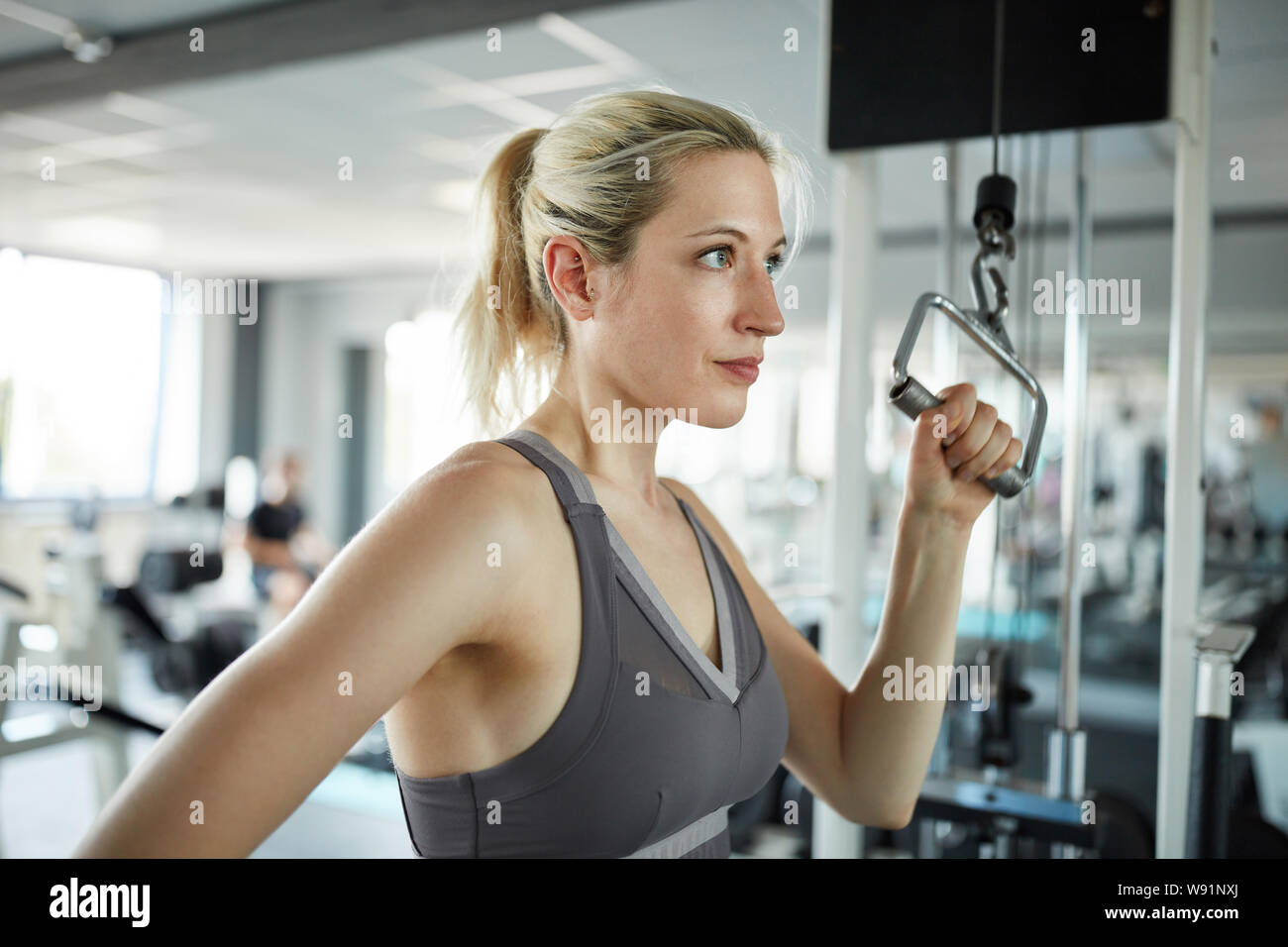 Sporty young woman trains triceps muscle on cable in fitness center ...