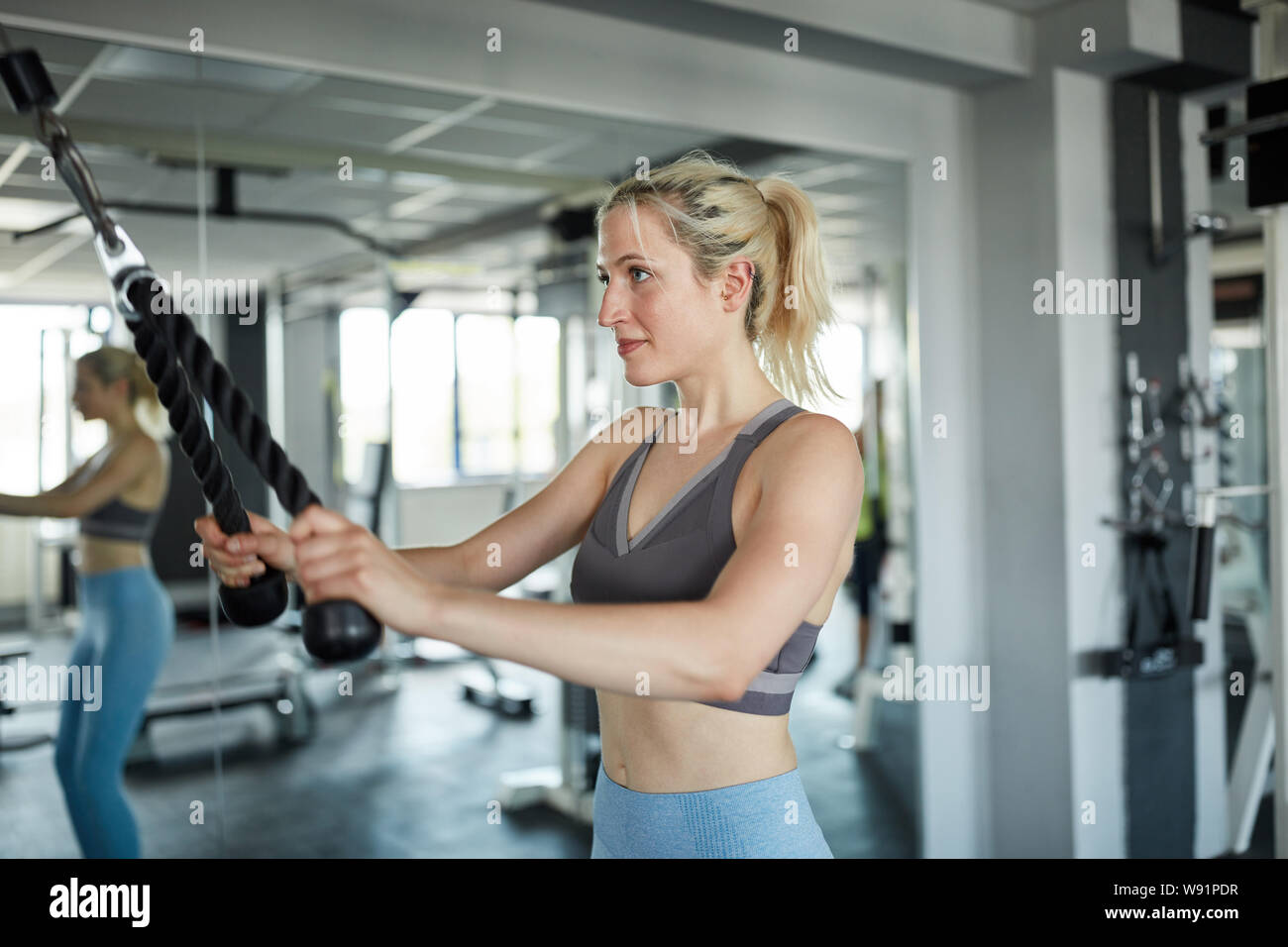 Young woman in bodyshaping at train station exercises with triceps rope ...