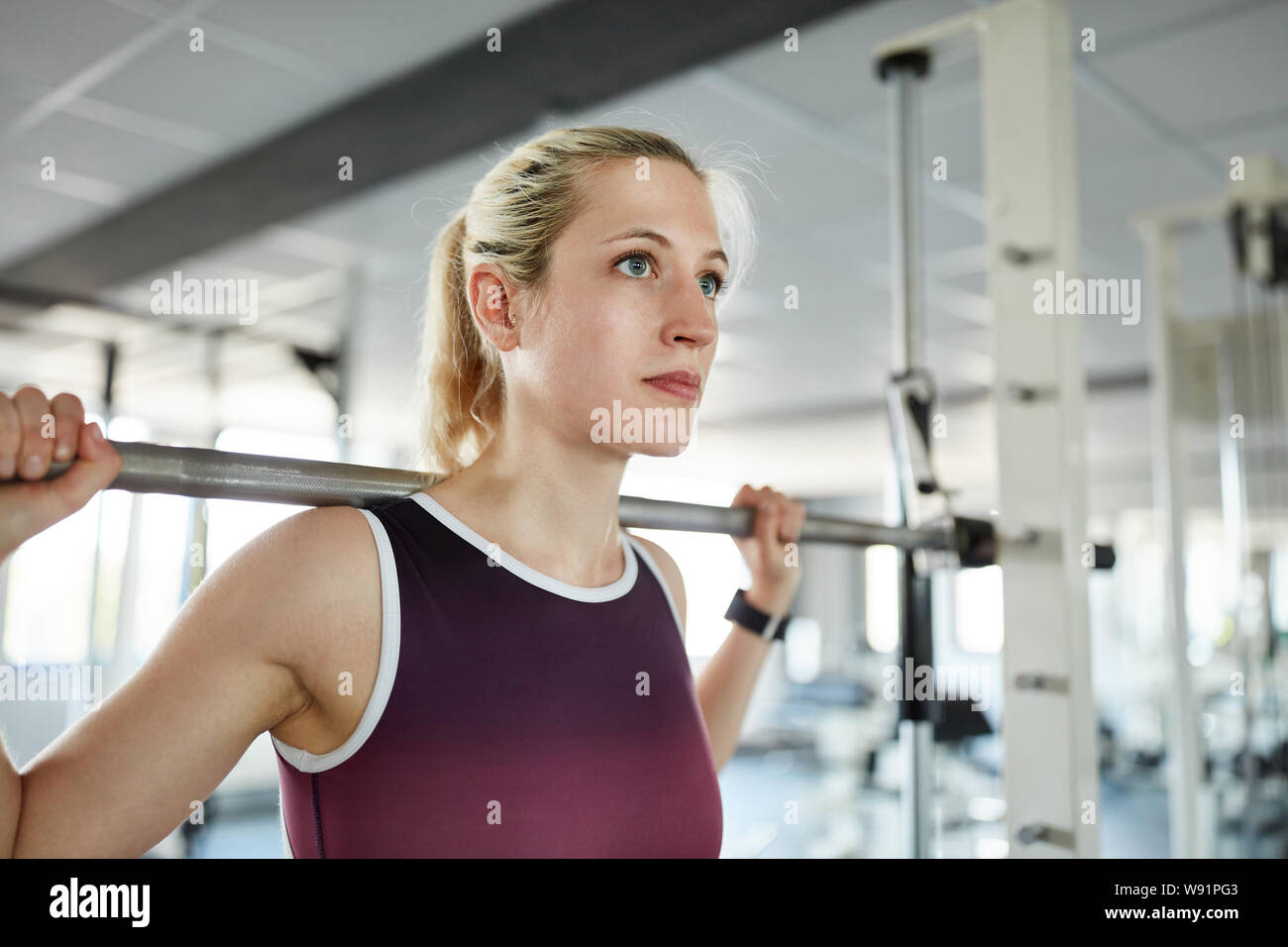 Young woman trains leg muscles in the barbell station in the fitness ...