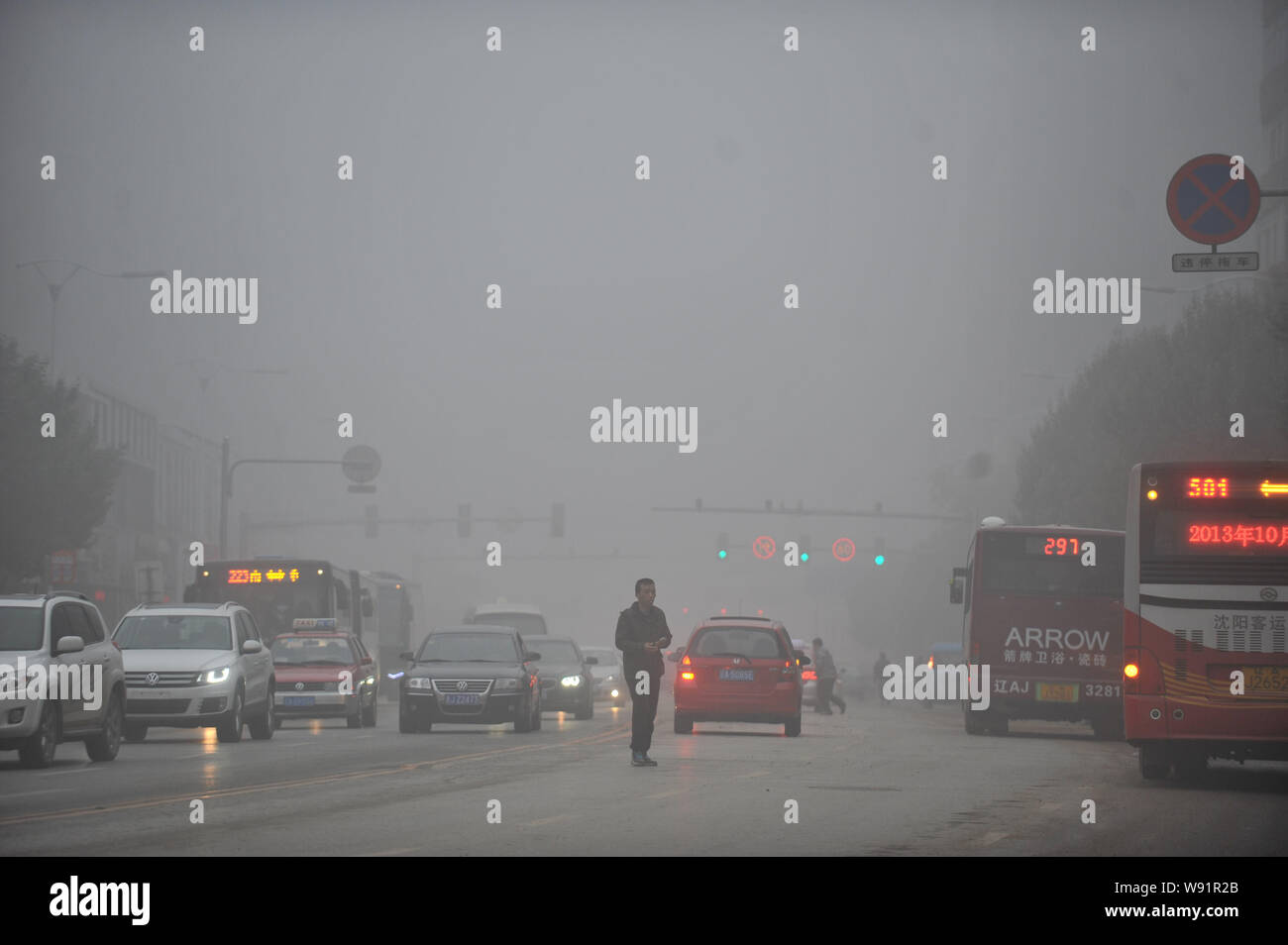 A pedestrian walks across a road among vehicles in heavy smog in ...