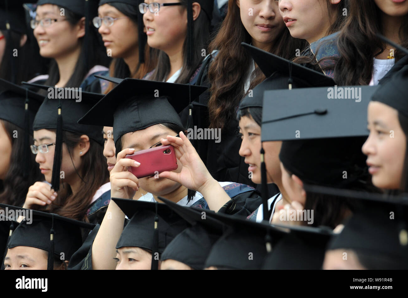 A Chinese graduate dressed in an academic costume takes photos of ...