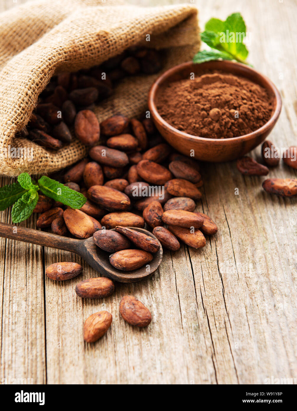 Raw cacao beans in burlap bag and bowl with cacao powder on a wooden ...