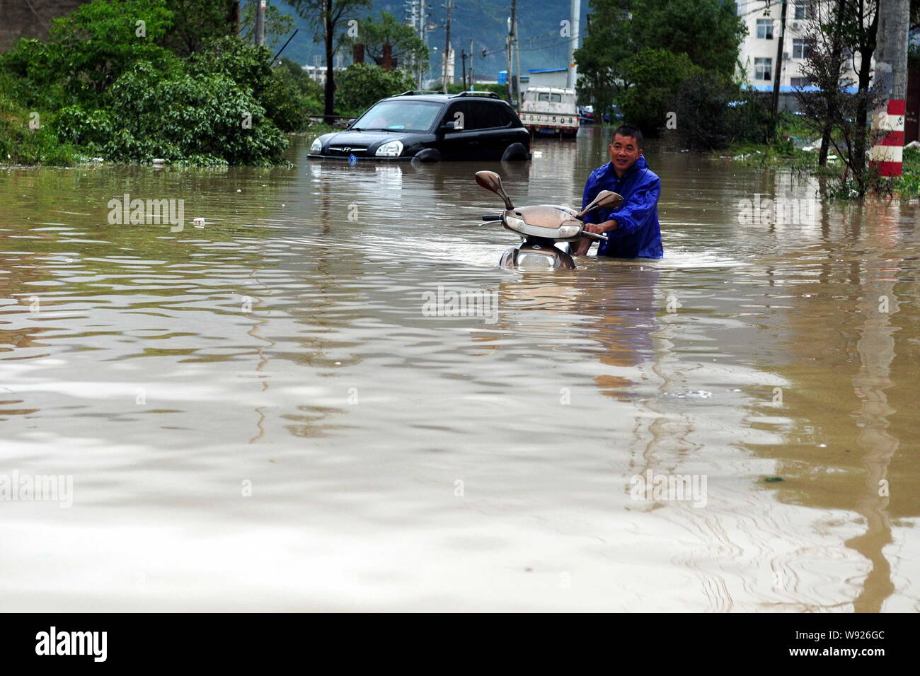 A Chinese cyclist pushes his electric bike on a flooded road after ...