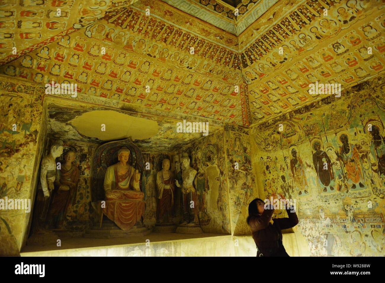 A visitor takes photos of replicas in a replicated chamber of the Mogao Grottoes during the ...