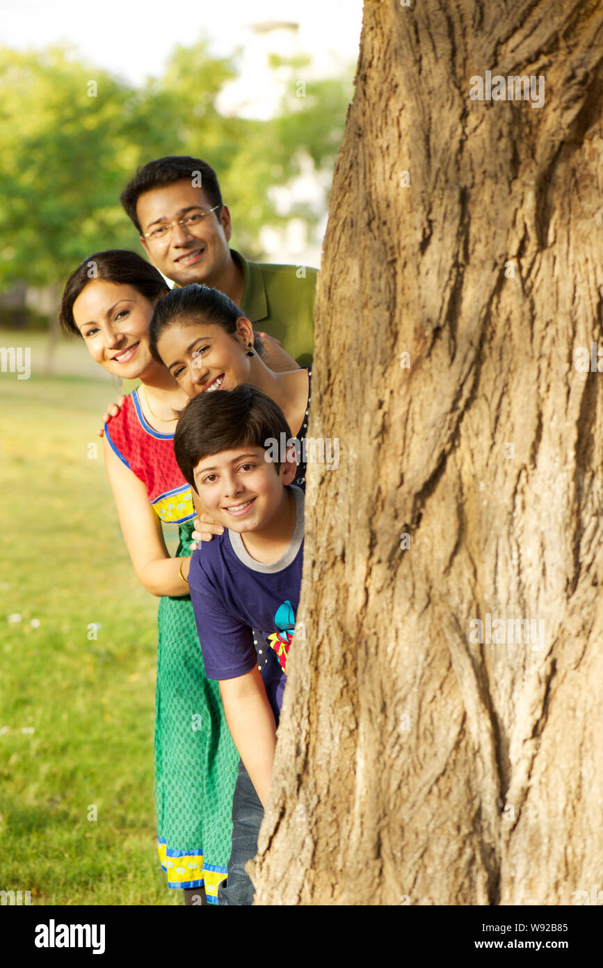 Family peeking out from behind tree Stock Photo - Alamy