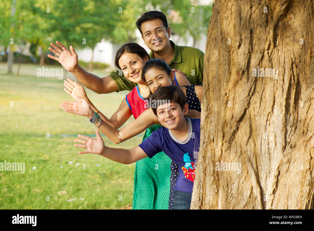 Family waving hands behind a tree Stock Photo - Alamy