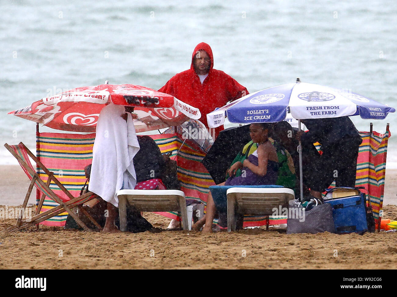 People shelter during heavy rain on the beach in Margate, Kent, as ...