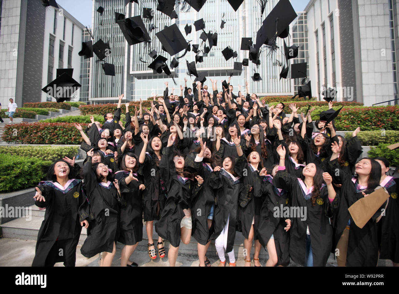 Chinese graduates dressed in academic costumes throw hats into the air ...