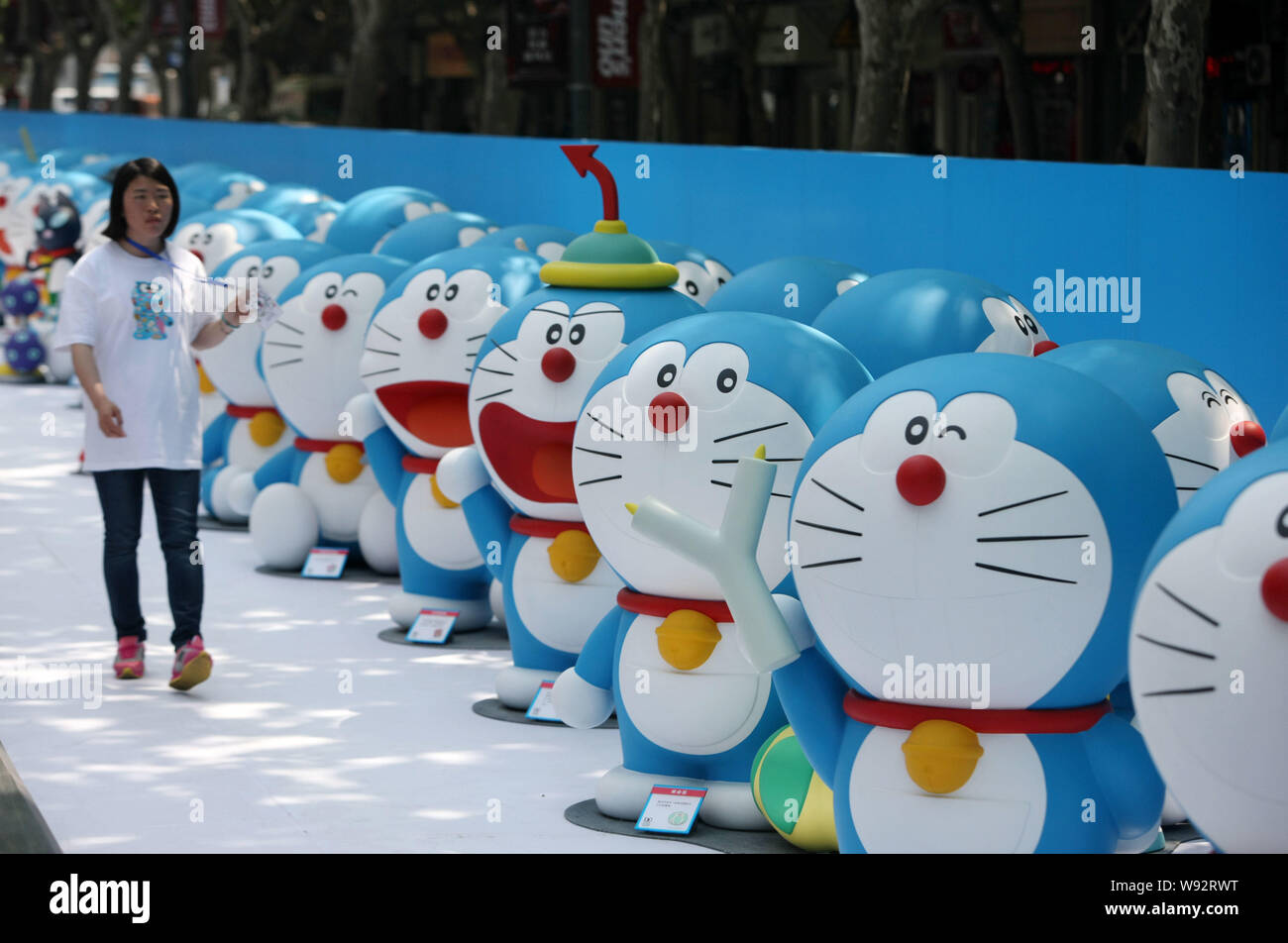 A Chinese employee walks past models of Doraemon, a famous Japanese ...