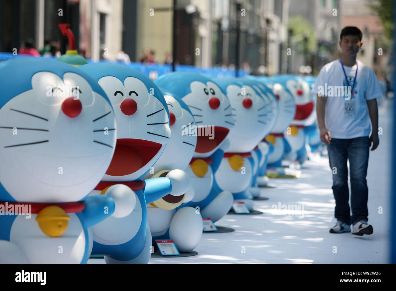 A Chinese employee walks past models of Doraemon, a famous Japanese ...