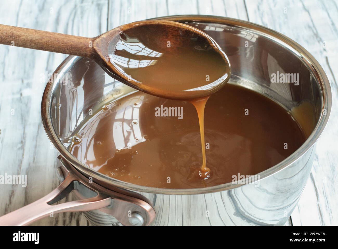 Wooden spoon dripping caramel sauce into a pan. Selective focus with ...