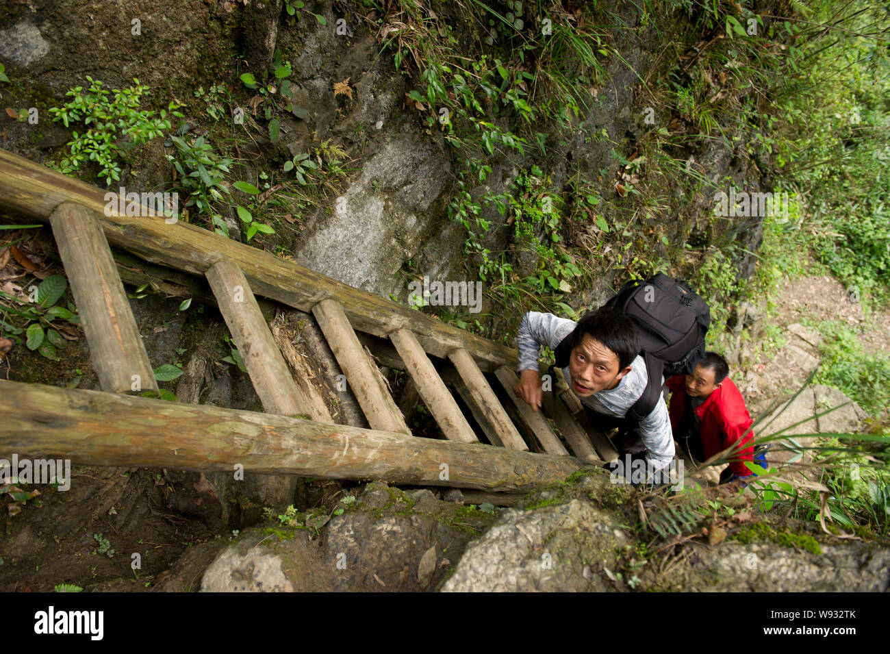--FILE--Chinese men climb a vertical wooden ladder on the cliff of a ...