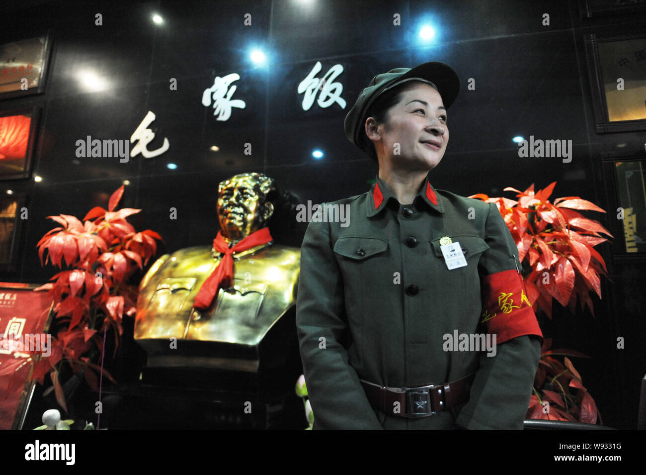 A waitress in red guard uniform welcomes customers in front of a bust ...