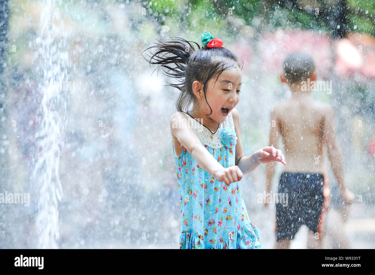 A young girl plays with water to cool down in a fountain on a scorching ...