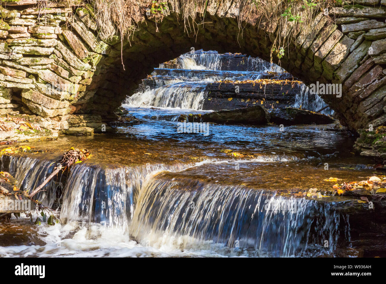 Waterfall under an old arch bridge Stock Photo - Alamy