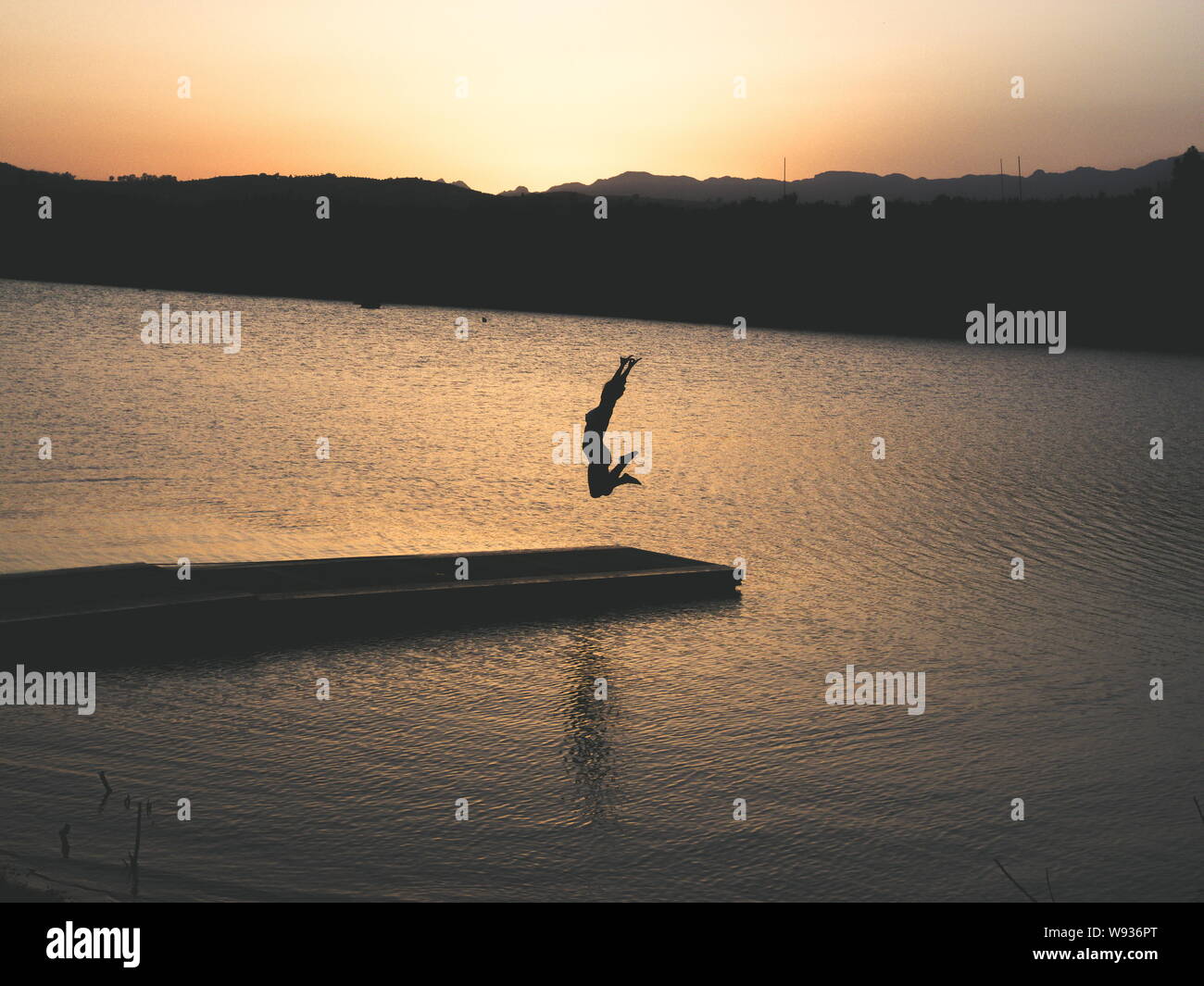 An adult woman jumping on a lake dock at sunset Stock Photo - Alamy