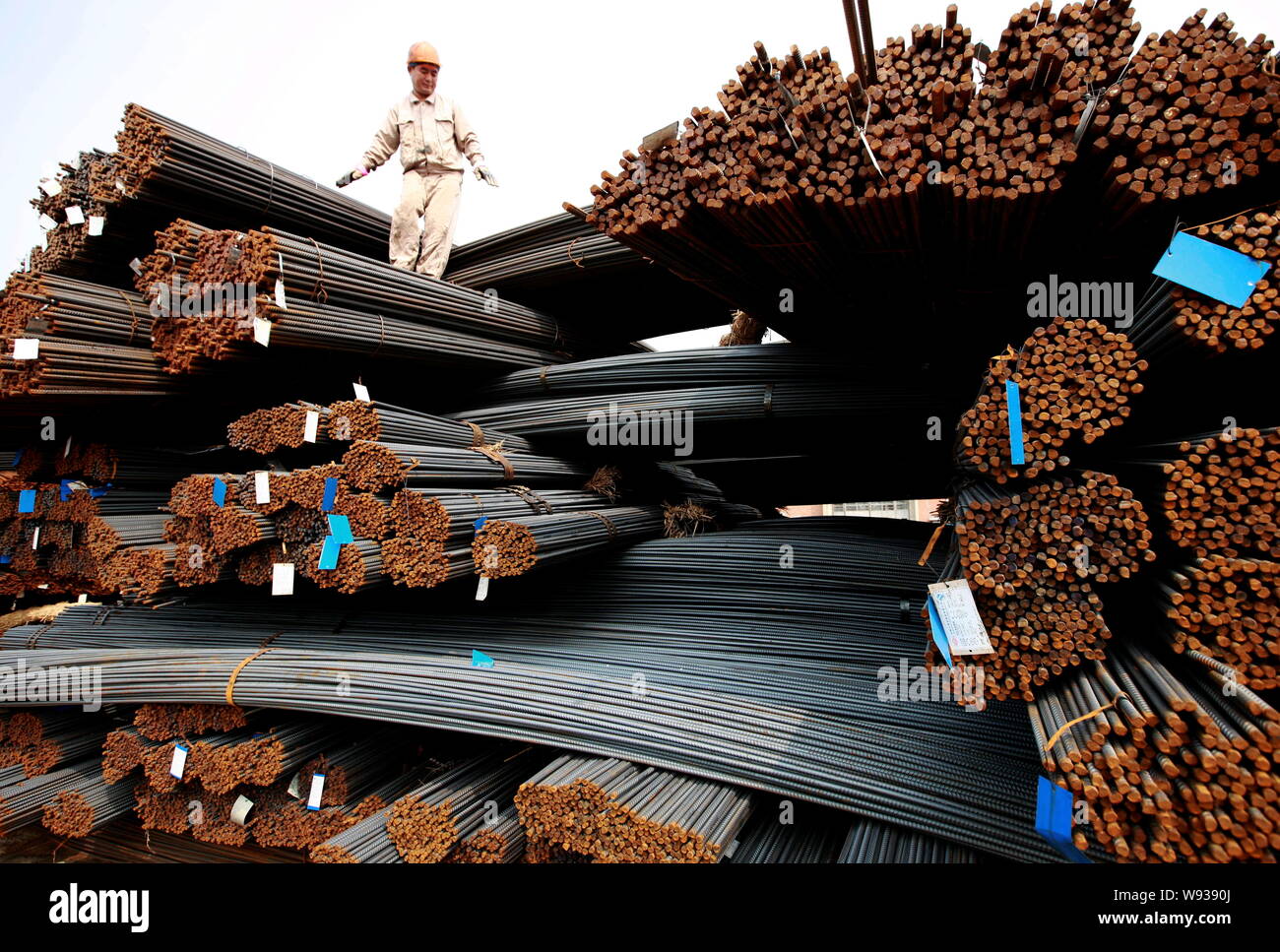 A Chinese worker stands on a stack of reinforcing steel rods at a steel ...