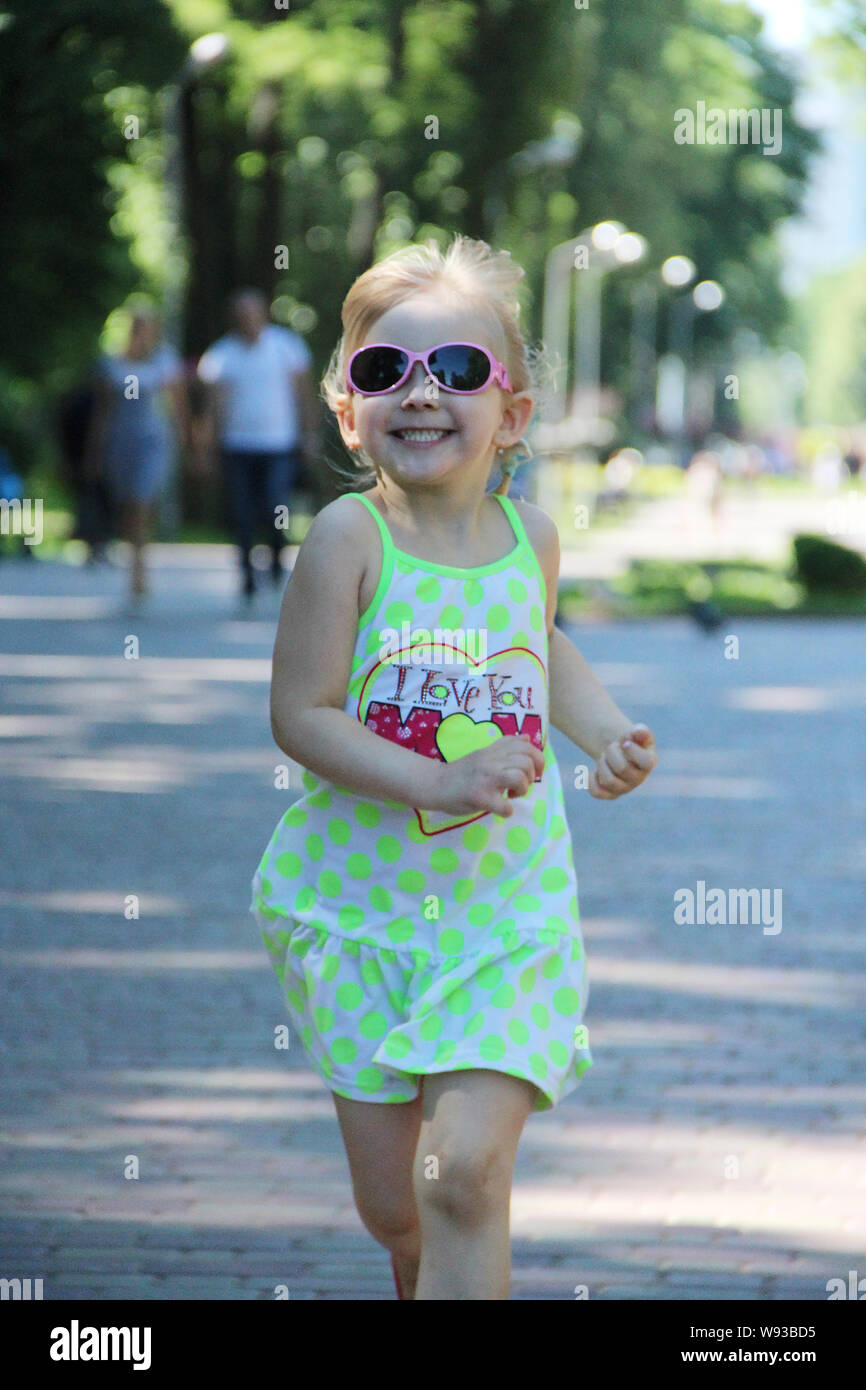 Happy little girl running in city park. Positive childish emitions ...
