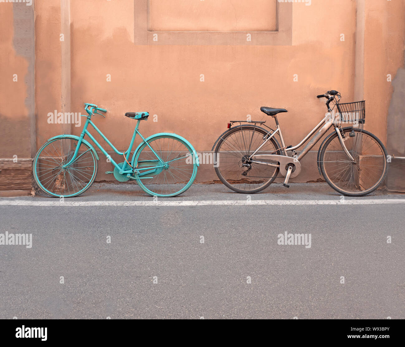 Two old bikes , turquoise and beige, leaning against the old, orange ...