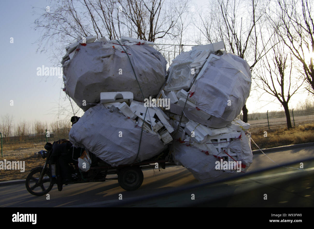 A motor tricycle overloaded with foamed plastics rides on a road in ...