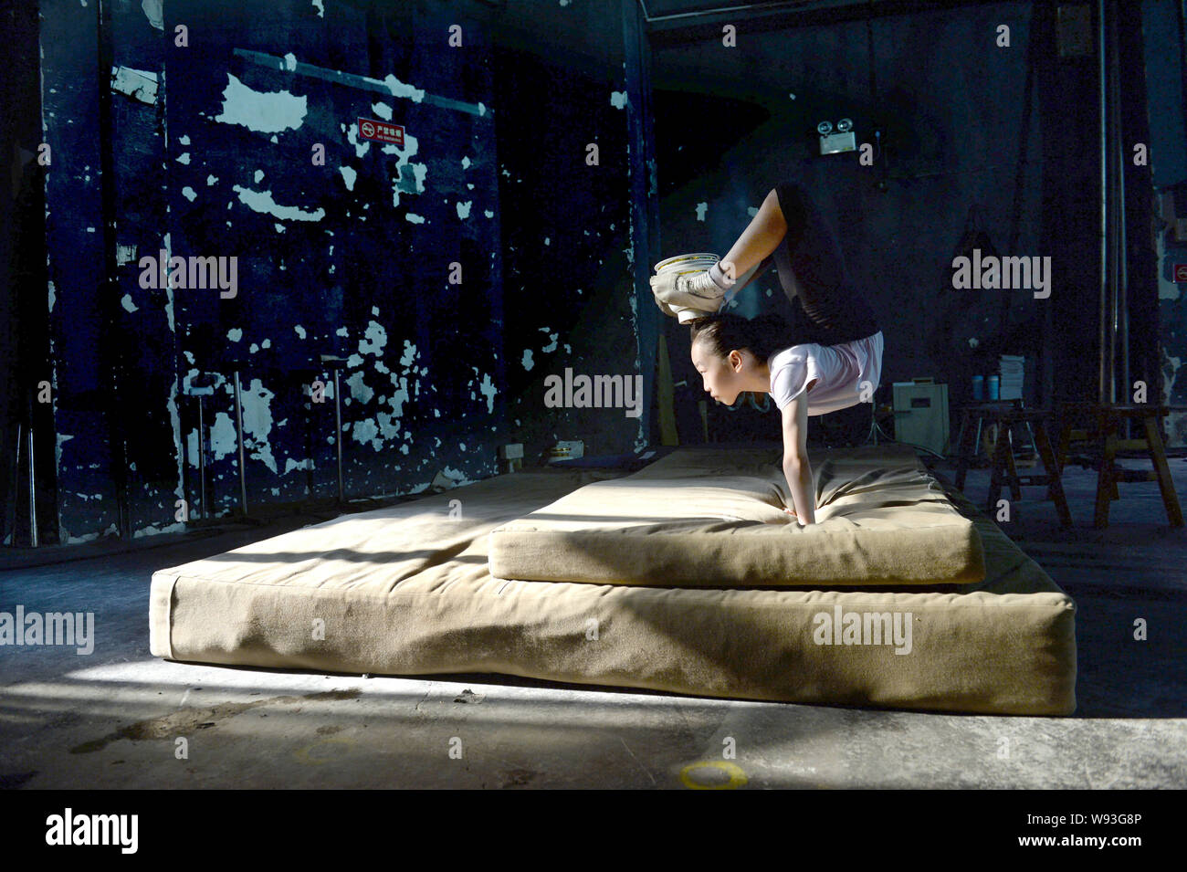 A young Chinese acrobat pratices as she hand-stands and bends her body ...