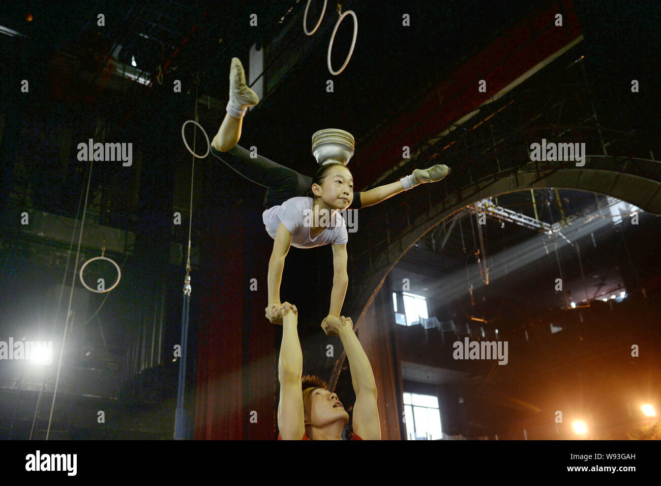 A young Chinese acrobat holds up a young girl as she bends her body and ...