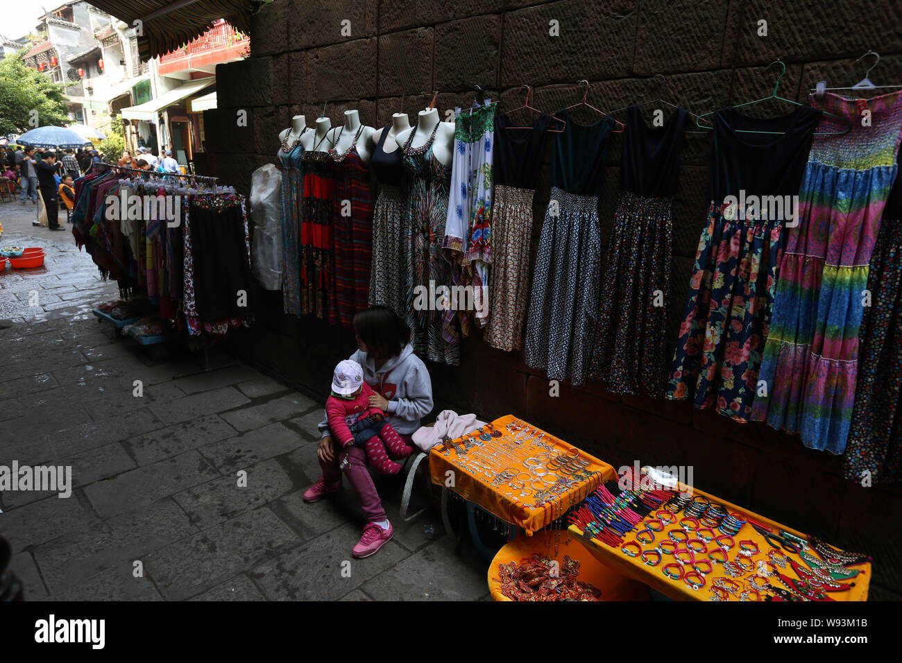 A Chinese store owner holds her son while sitting in front of her cloth ...