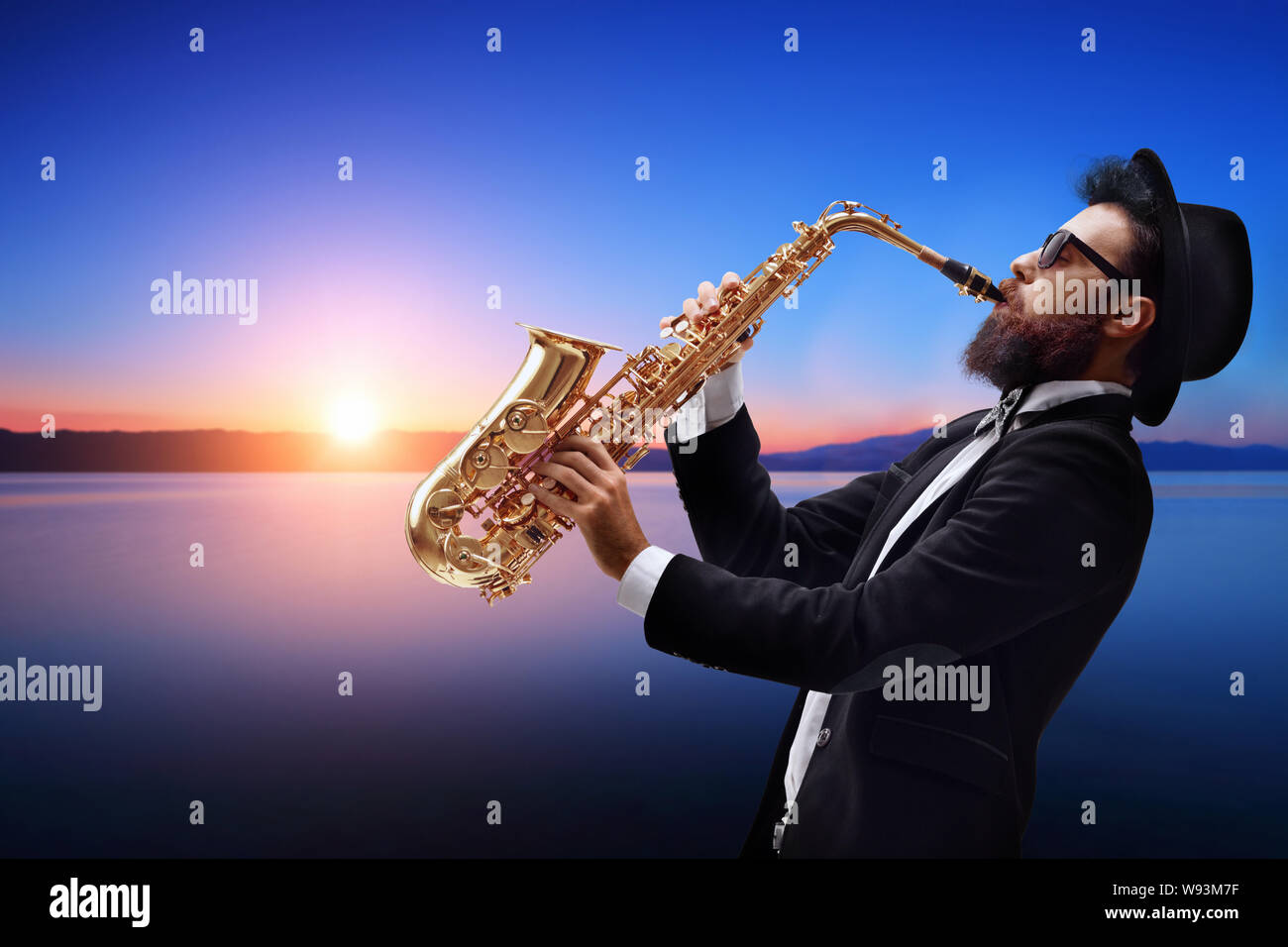 Male jazz musician playing a saxophone with a sunset and water behind ...