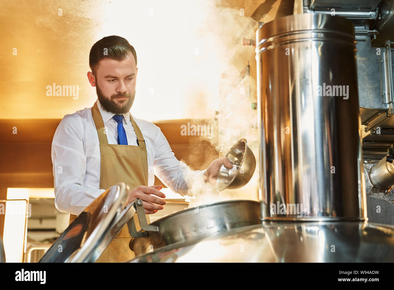 Serious man brewing beer. Professional brewer in white shirt and apron ...