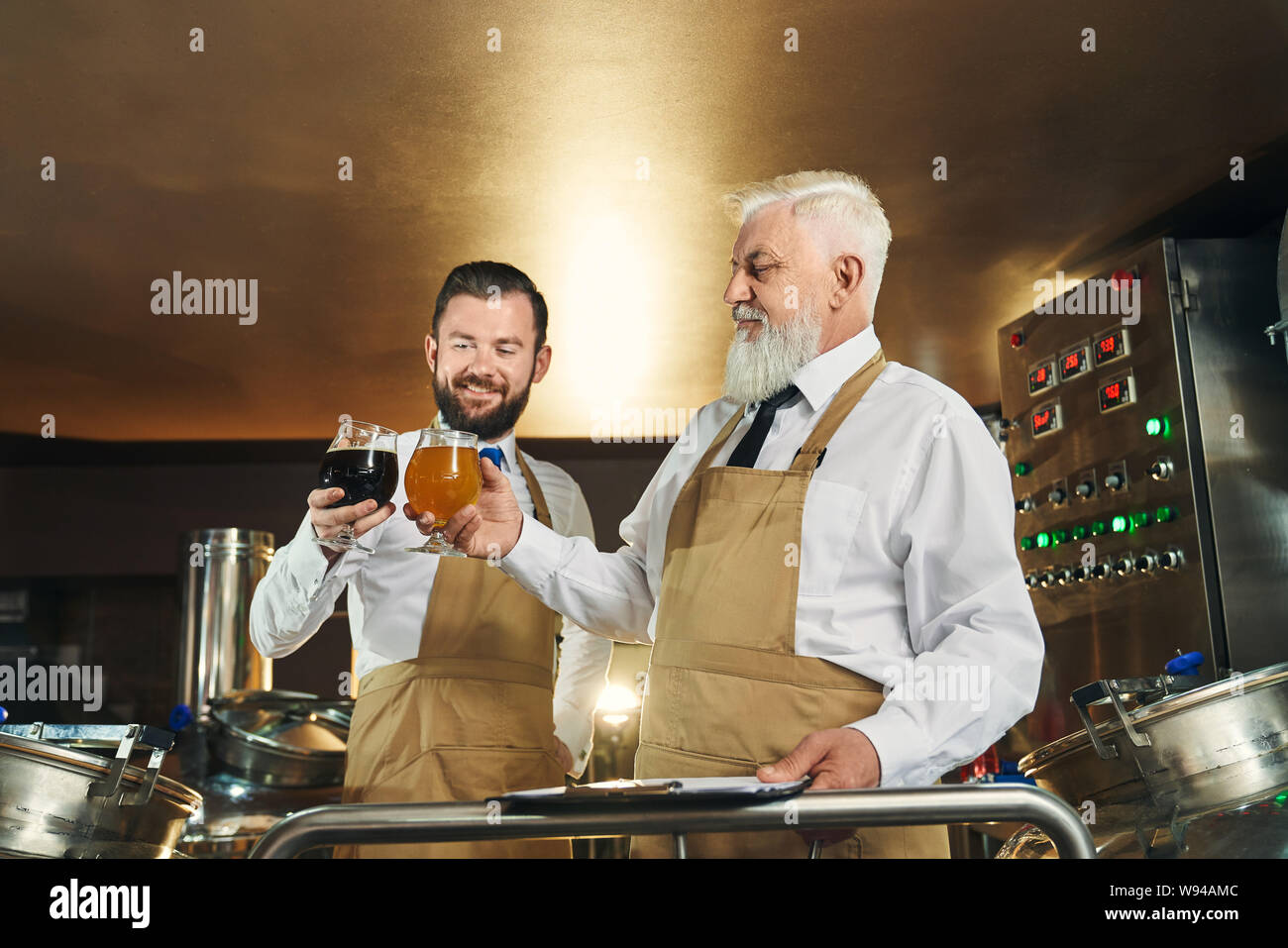 Two male brewers keeping glasses with dark and light beer and toasting ...