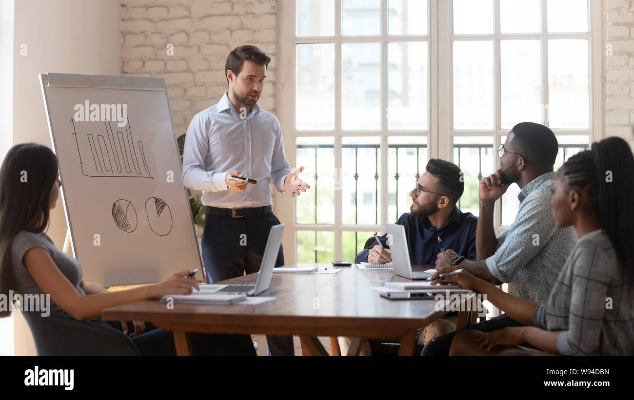 Serious male coach give flip chart presentation to diverse employees ...